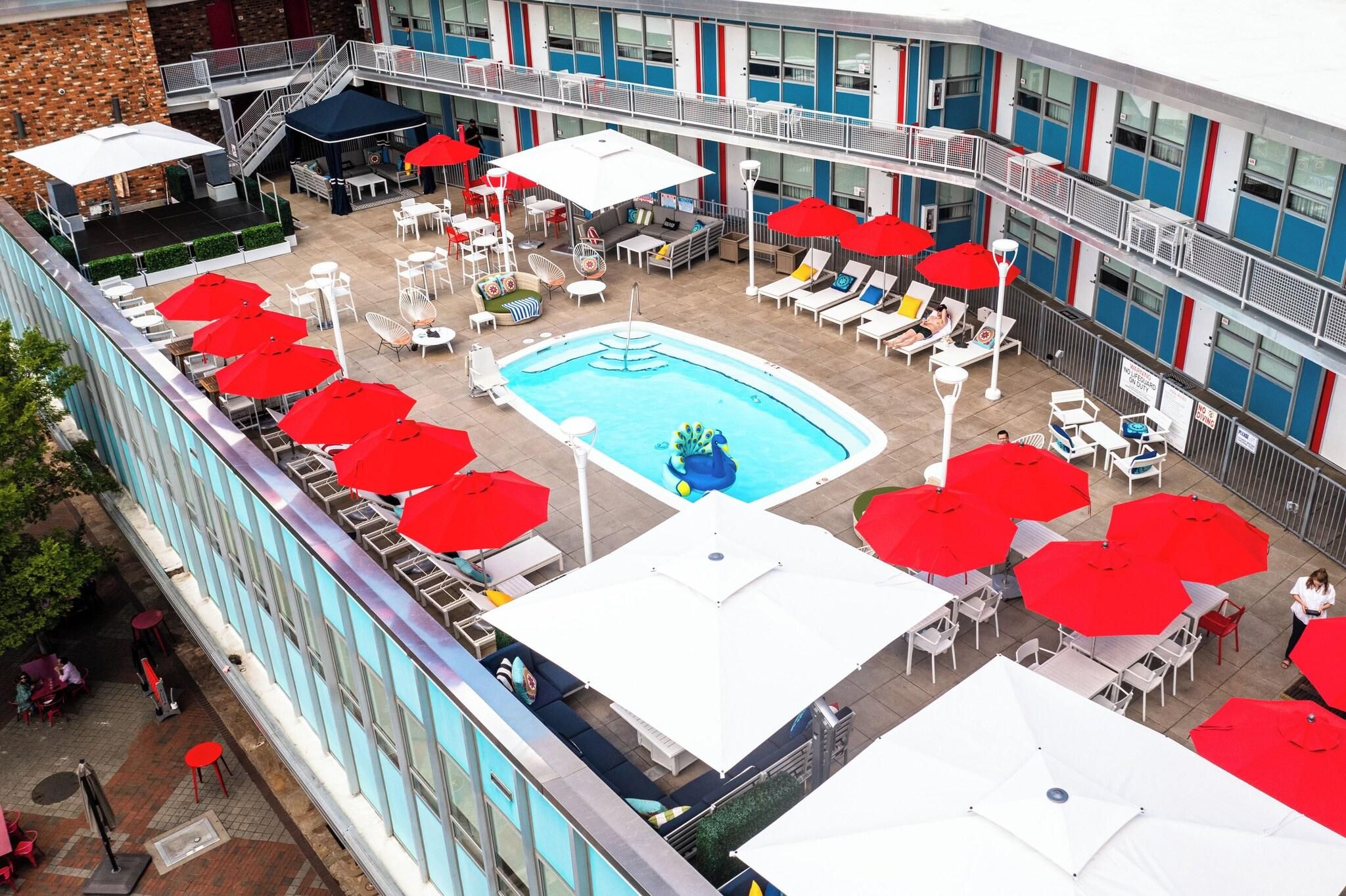 Uma área de piscina no terraço com vários guarda-sóis vermelhos, espreguiçadeiras e uma piscina central.
