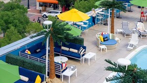 Uma área de piscina no terraço com espreguiçadeiras, guarda-sóis e vista para os edifícios ao redor.