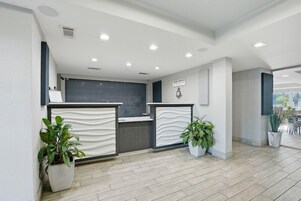 Uma área de recepção com design moderno, destacando um balcão de atendimento, plantas em vasos e uma placa visível na parede.