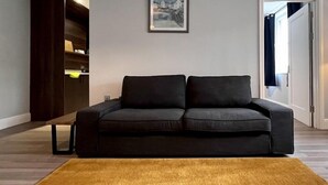 Uma sala de estar moderna com um sofá preto, um quadro na parede e chão de madeira.