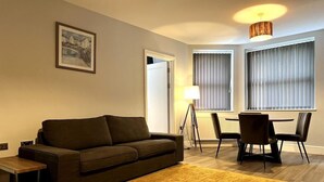 Uma sala de estar com sofá, mesa de centro, luminária e um espaço de jantar com cadeiras.