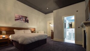 Quarto com uma cama grande, mesas de cabeceira, um criado-mudo, um quadro na parede e uma porta que dá para um banheiro.