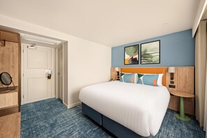 Quarto de hotel com uma cama grande, um guarda-roupa de madeira, um espelho redondo e uma pequena mesa redonda.