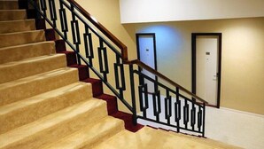 Uma escada com carpete e guarda-corrimão de metal preto que leva a uma porta.