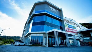 Um hotel moderno com um destaque para a placa "Ancyra Hotel", fachada de vidro ampla e uma placa "Post City Mall" indicando compras próximas.