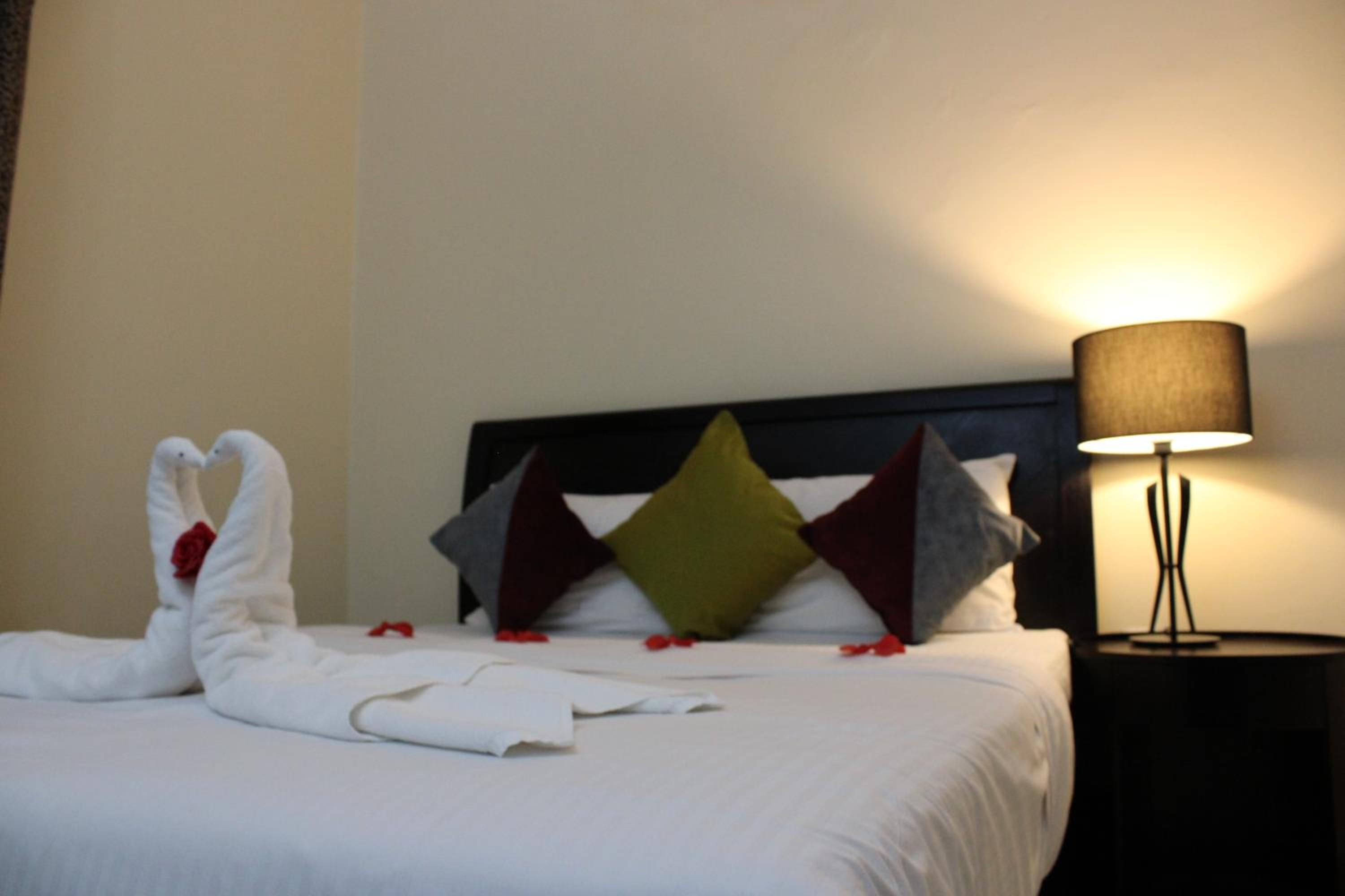 Uma cama bem arrumada com edredom branco, almofadas decorativas e uma luminária em uma mesinha de cabeceira.