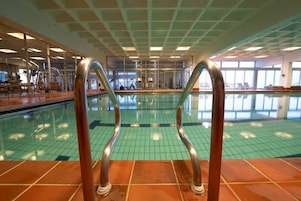 Piscina interna com água cristalina, cercada por piso e paredes revestidas, e equipada com escadas de metal.