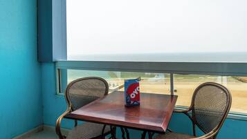 Uma mesa com um saco de snacks OYO, duas cadeiras de vime e vista para a praia através de uma janela.
