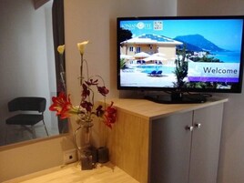 Uma área de recepção com televisão exibindo uma tela de boas-vindas, um vaso com flores e um balcão de madeira.
