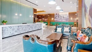Um hall de hotel com balcão de recepção, área de estar e estante de livros.