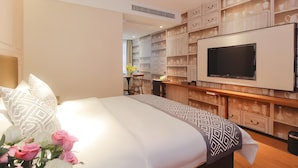 Quarto moderno com uma cama grande, TV fixada na parede e armários embutidos.