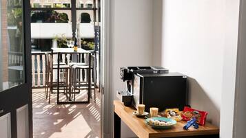 Quarto com máquina de café, mesa com prato de comida e janela com vista para uma varanda com cadeiras.
