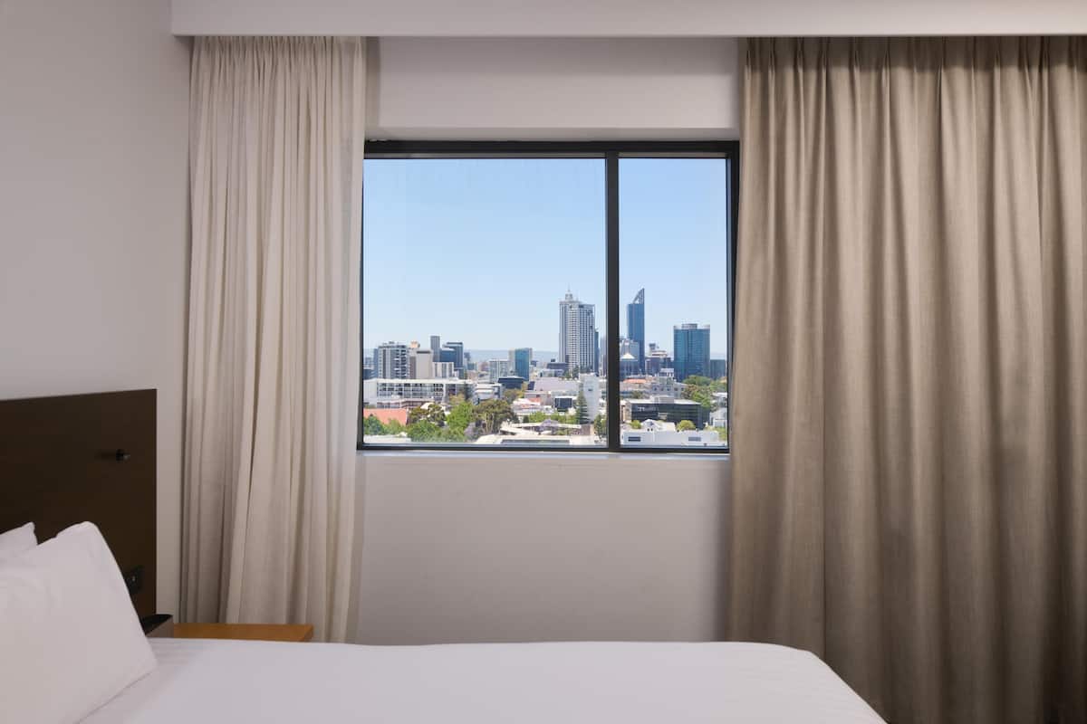 Quarto de hotel com uma grande janela, uma cama e cortinas.