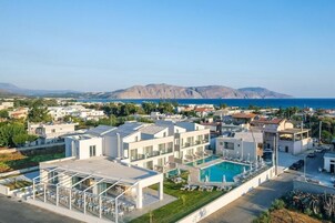 Resort costeiro com edifícios modernos, piscina e vista para o mar e montanhas.