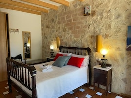 Quarto com parede de pedra, estrutura de cama de madeira e duas luminárias de cabeceira.