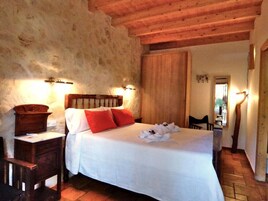 Um quarto com cabeceira de madeira, colcha branca, almofadas vermelhas e mesa de cabeceira de madeira com uma luminária.