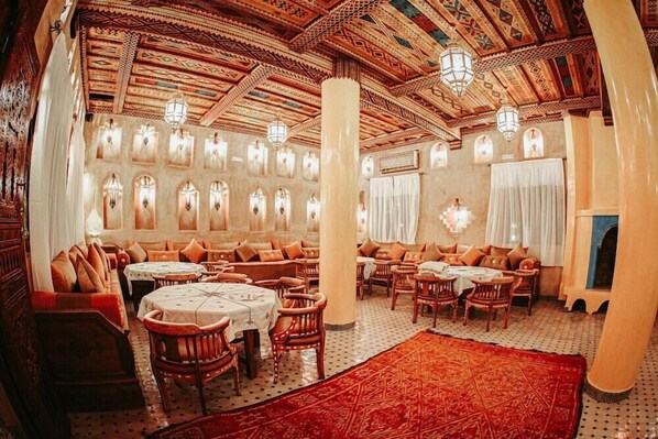 Um interior luxuoso com tetos de madeira ricamente decorados, vários espaços para sentar e tapetes estampados.