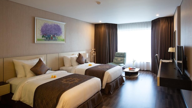 Quarto de hotel com duas camas, uma escrivaninha, uma cadeira, uma televisão e um quadro na parede.