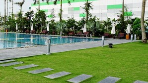 Uma piscina com cachoeira, rodeada por um gramado bem cuidado e palmeiras.