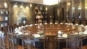 Uma mesa redonda grande com cadeiras, rodeada por estantes de livros e um objeto decorativo na parede.