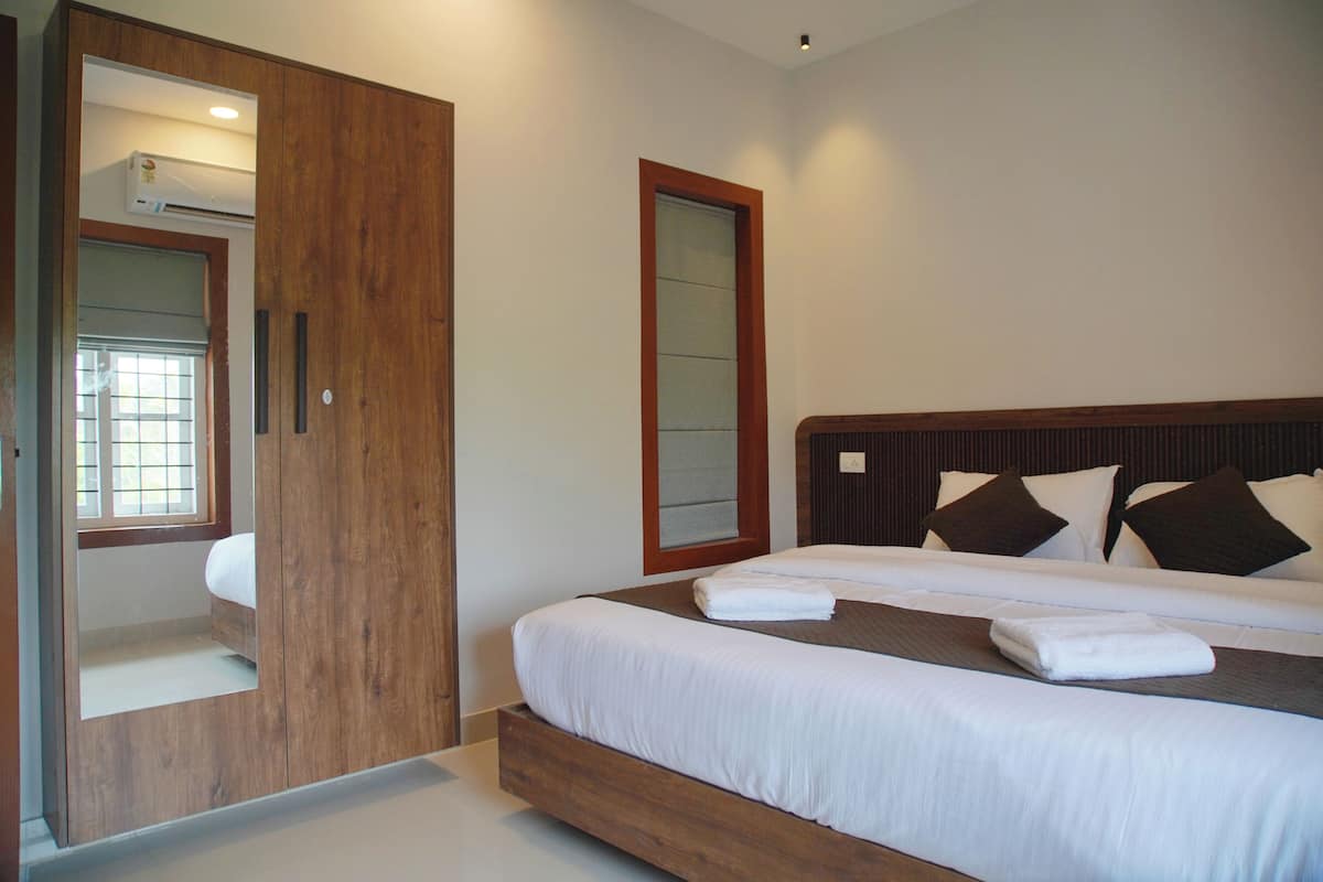 Quarto com duas camas, um guarda-roupa de madeira, um espelho e uma janela com persianas.