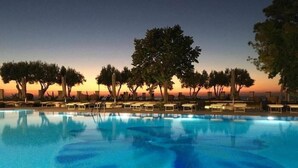 Piscina com espreguiçadeiras e árvores ao fundo ao crepúsculo.