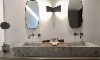 Uma casa de banho moderna com uma lavatório de mármore retangular, dois espelhos fixados na parede e um espelho redondo pequeno.