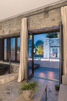 Um interior moderno com uma parede de pedra, uma banheira preta e vista para uma área de piscina externa.