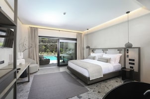 Quarto de hotel moderno com uma cama grande, uma mesa, uma cadeira e vista para uma piscina.