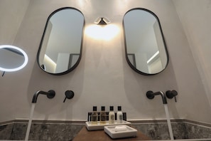 Casa de banho com dois espelhos grandes, uma luz na parede e toucador com bancada de mármore.