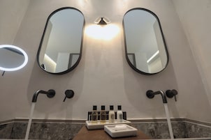 Casa de banho com dois espelhos grandes, uma luz na parede e toucador com bancada de mármore.