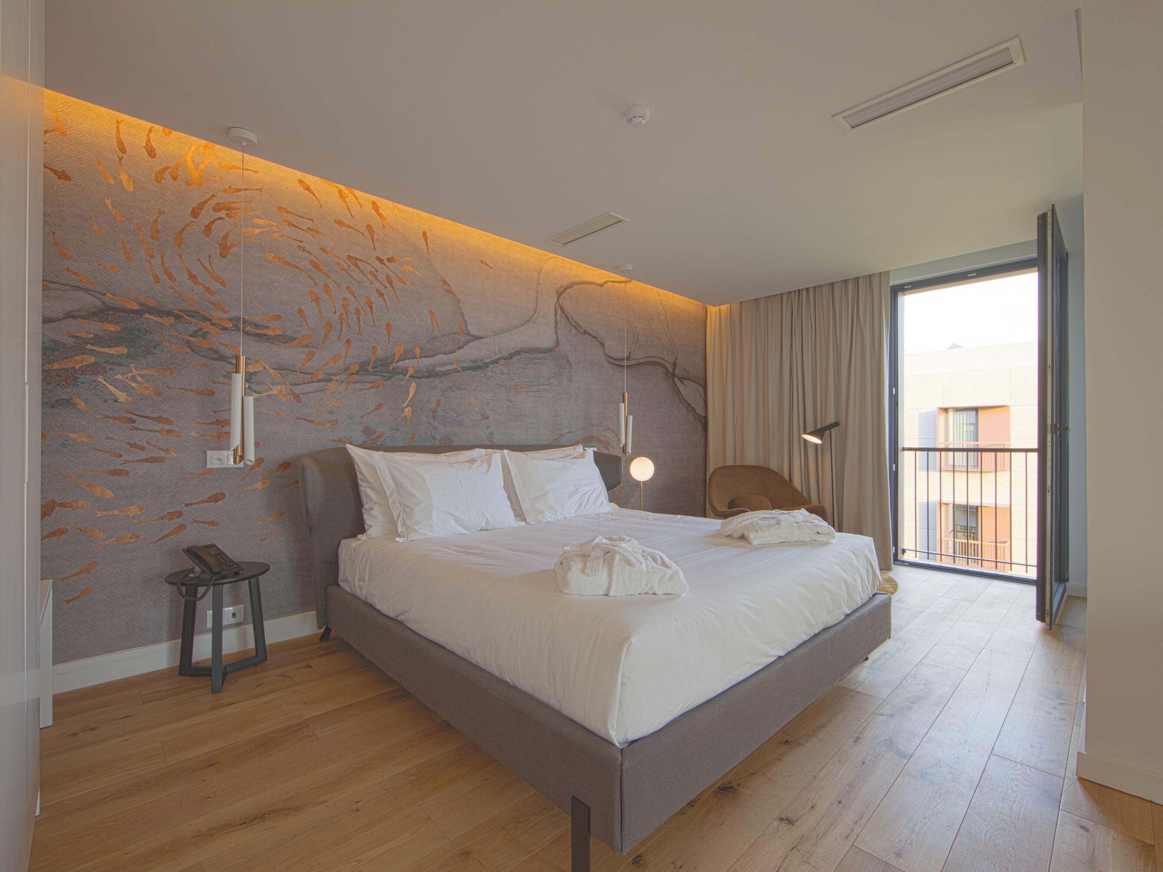 Quarto moderno com uma cama grande, mesa de cabeceira, uma cadeira e vista para a varanda.