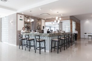 Uma área de bar moderna com bancada de mármore, vários bancos altos e um barista preparando bebidas.