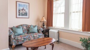 Quarto com sofá floral, mesa de madeira, luminária, radiador e janela com cortinas.
