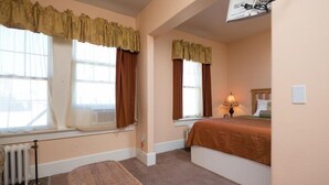 Quarto com cama, mesa de cabeceira, abajur e radiador.