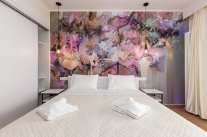 Quarto de hotel moderno com uma cama grande, roupa de cama branca e um mural texturizado na parede.