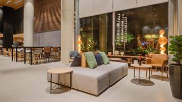 Um espaço interior moderno com sofá, mesas redondas e cadeiras dispostas para refeições ou relaxamento.