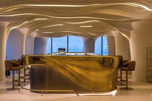 Uma área de bar moderna com balcão curvo, banquetas e um design de teto singular.