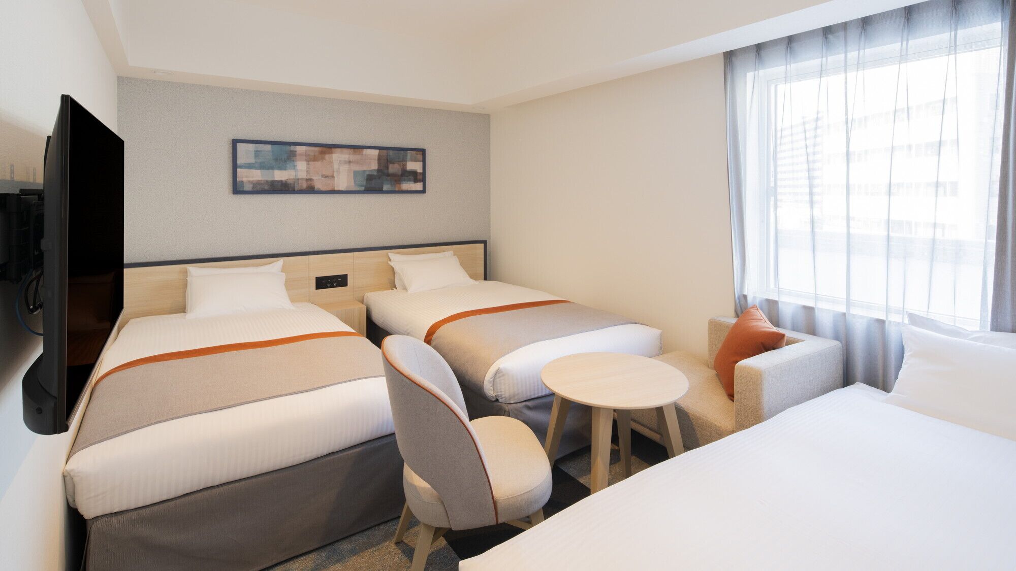Quarto de hotel com duas camas, uma televisão, uma mesinha e uma janela com cortinas.