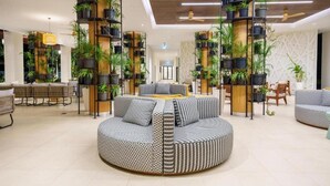 Uma área de estar moderna com sofá circular, diversas opções de assento e prateleiras verticais para plantas.