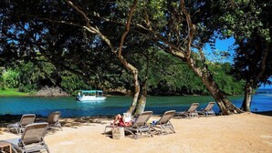 Uma praia com espreguiçadeiras e um barco ao fundo.