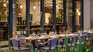 Um restaurante com uma mesa comprida posta para refeição, rodeada por cadeiras de vime.