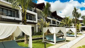 Um resort com edifícios de vários andares, áreas de estar ao ar livre com toldos brancos e palmeiras.