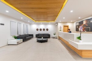 Uma área de recepção moderna com teto de madeira, dois sofás, um balcão de atendimento e uma janela ampla.