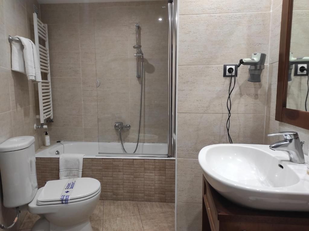 Uma casa de banho moderna com chuveiro em cabine de vidro, sanita branca e lavatório grande.