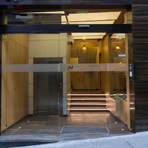 Entrada de hotel com design moderno, destacando uma porta de vidro, uma escadaria que leva ao interior e uma placa sobre a porta.