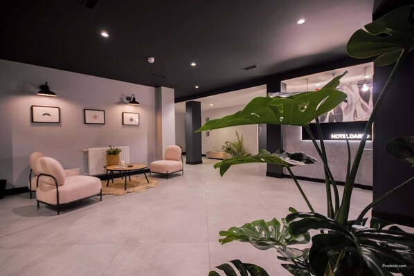 Um hall de hotel moderno com balcão de recepção, área de estar e plantas grandes.