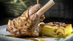 Paleta de cordeiro com molho e batatas assadas num prato.