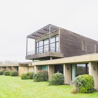 Um edifício moderno com telhado plano, janelas grandes e uma varanda.