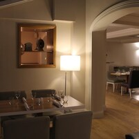 Uma sala de jantar com uma mesa posta para quatro pessoas, uma luminária e um espelho na parede.